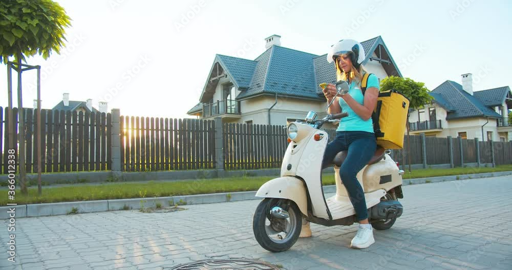 Beautiful young female courier riding on a scooter in safety helmet ...