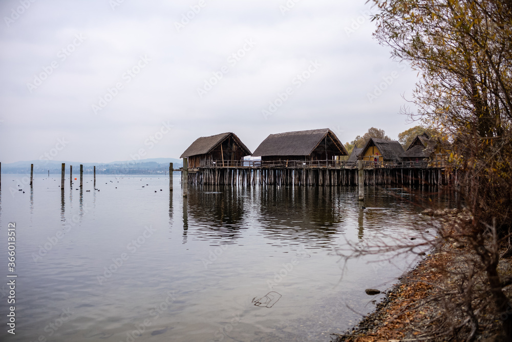 Bootshäuser auf Pfählen an einem See in den Alpen, im Hintergrund ...