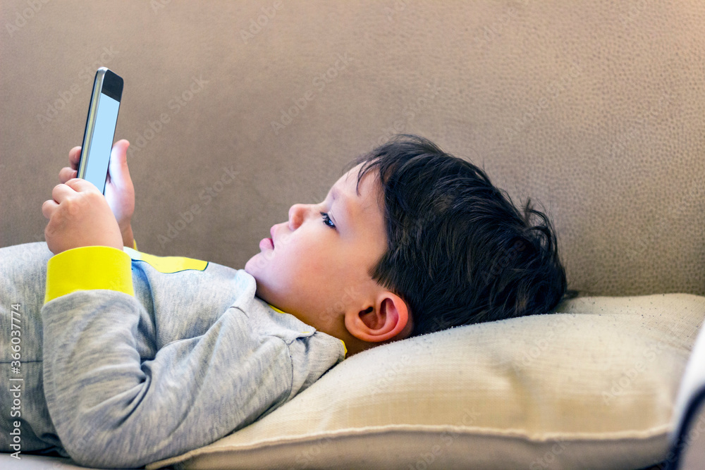 Boy playing smartphone on bed, watching smartphone, young boy use phone ...