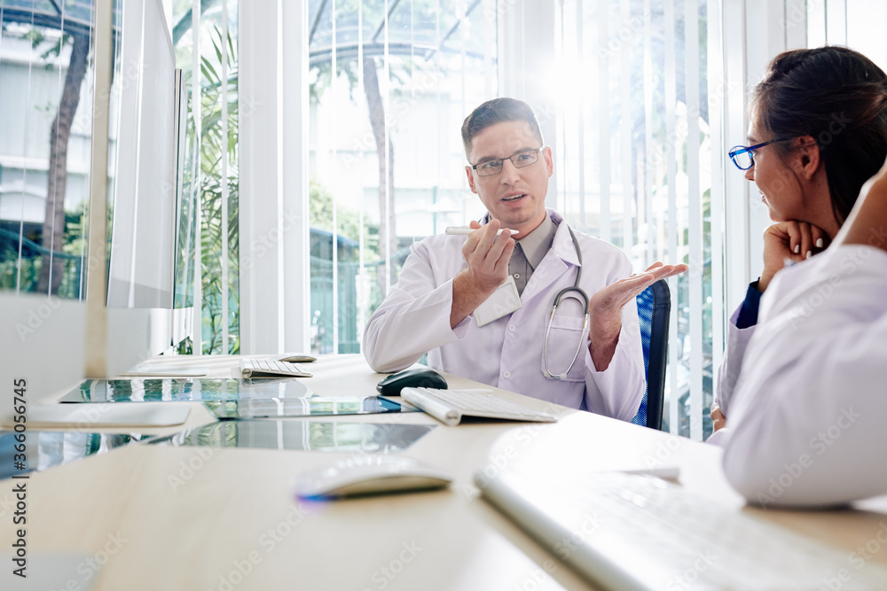 Serious young general practitioner talking to young female colleagues ...