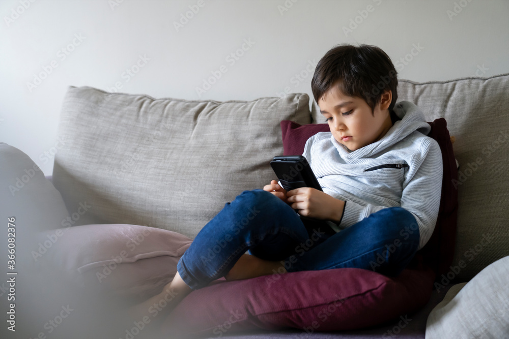 Child boy sitting on sofa watching cartoons on mobile phone, School kid ...