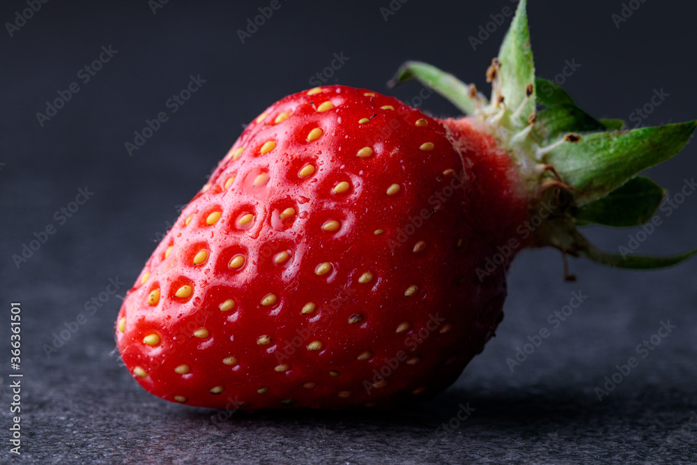 one red strawberry fruit with fine splashes on dark grey background ...