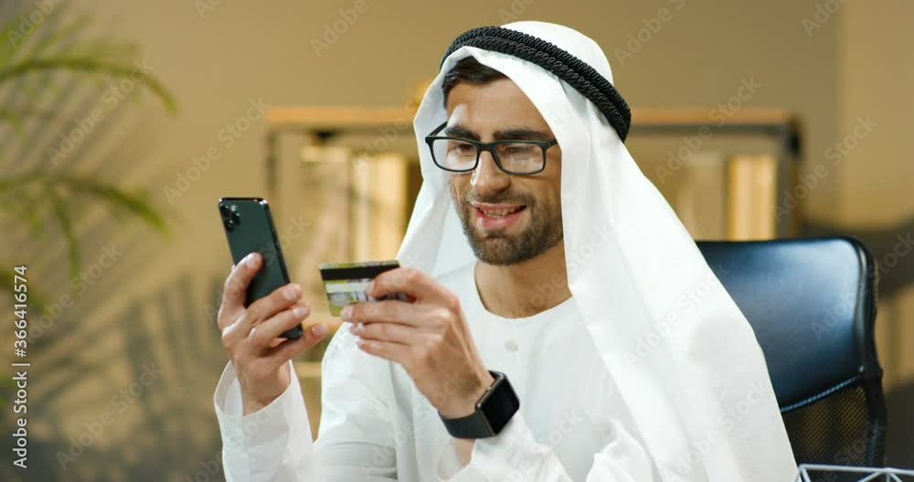 Young happy muslim man in traditional emirates outfit shopping online ...