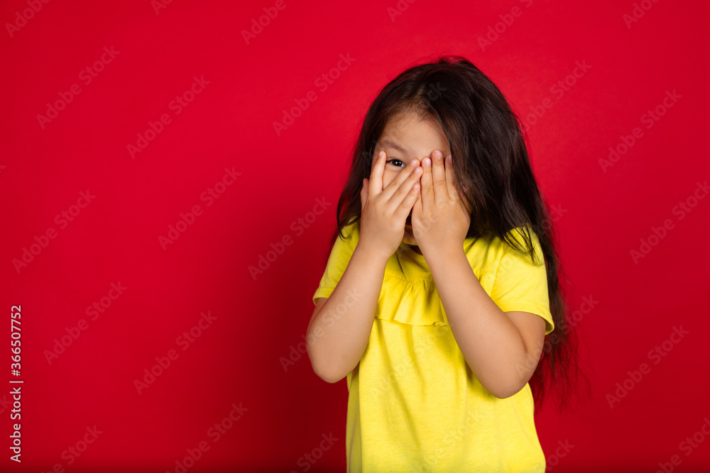 Scared hiding face with hands. Beautiful little girl on red background ...