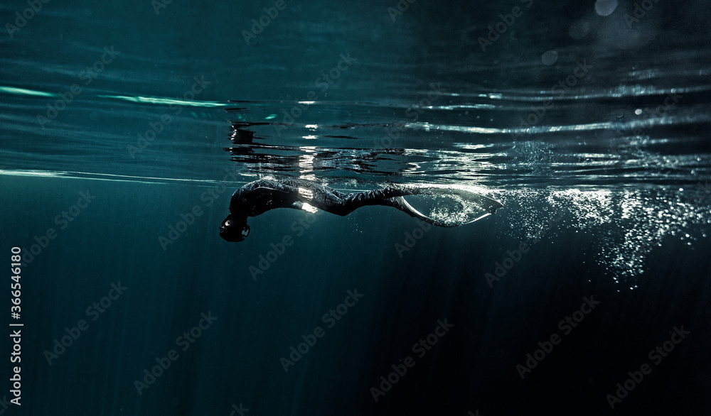 Underwater view of diver wearing wetsuit and flippers diving just below ...