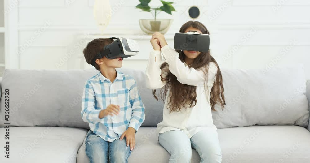 Caucasian small cute kids in VR glasses sitting on white sofa in living ...