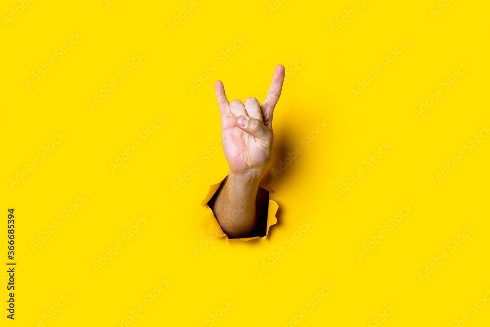 Male hand shows the gesture of goat, rocker goat, horns on a yellow ...