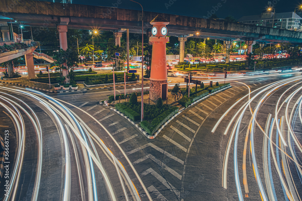 Car lights at night on the road going to the city with clock tower time ...