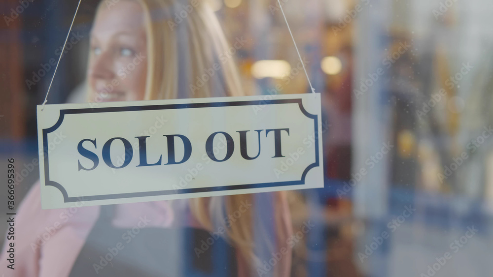 Cheerful senior female bakery owner hanging sold out sign on glass door ...