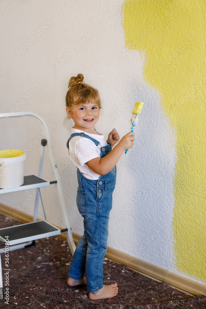 Cute little toddler girl painting the wall with yellow color in new ...