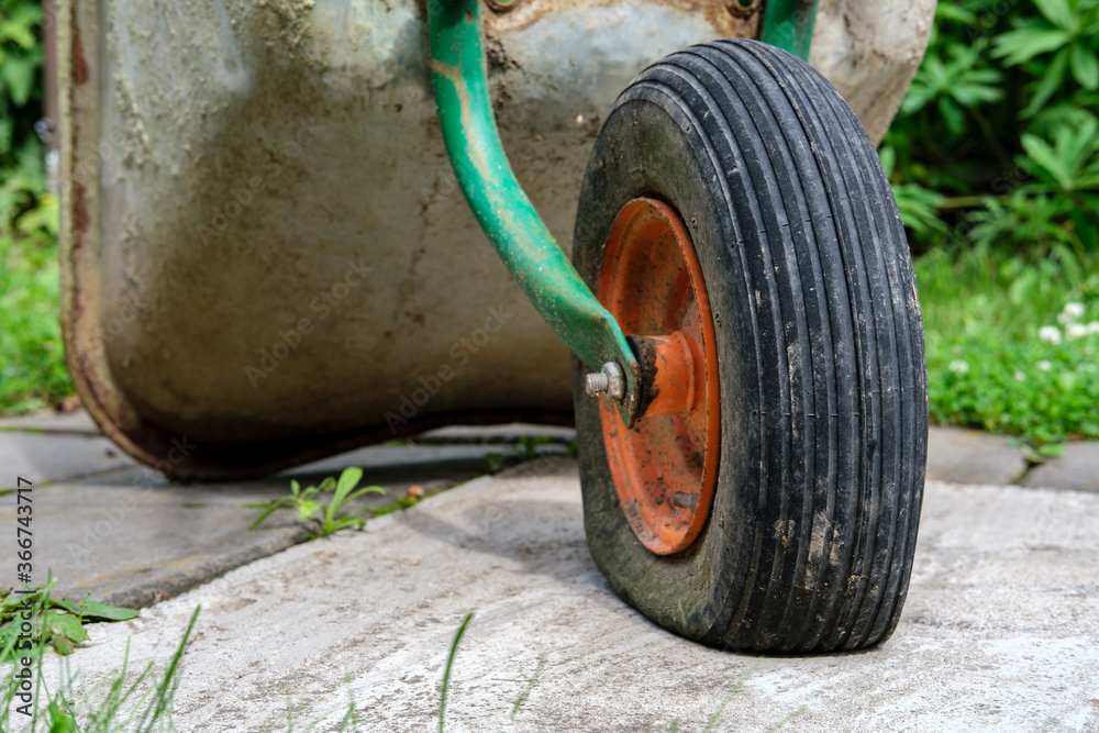 A wheel of an old and rusty garden wheelbarrow, deflated by a puncture ...