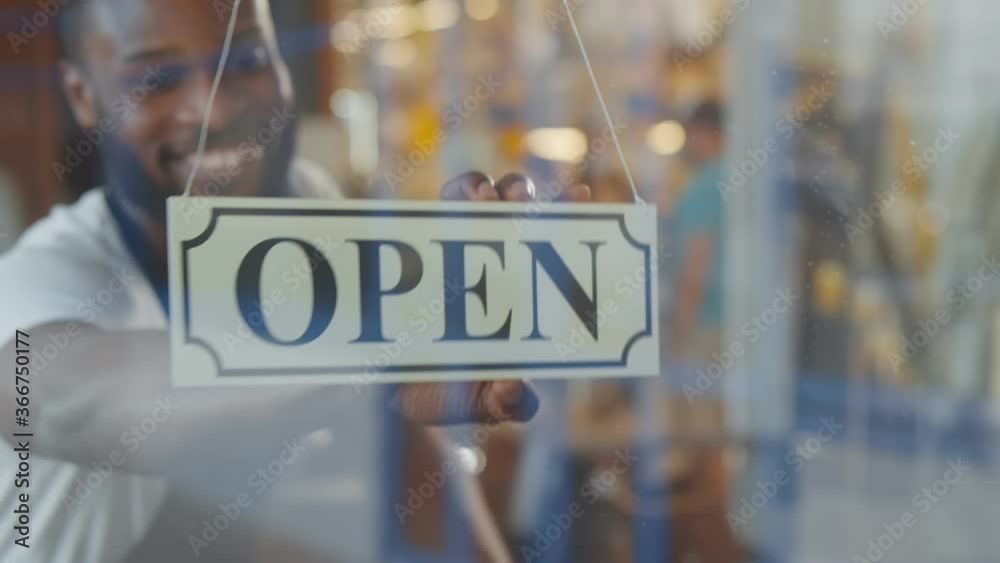 Smiling african waiter closing restaurant for break turning closed sign ...