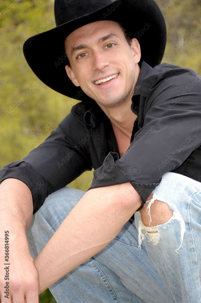 Handsome cowboy squats for a fun country portrait with a big black ...