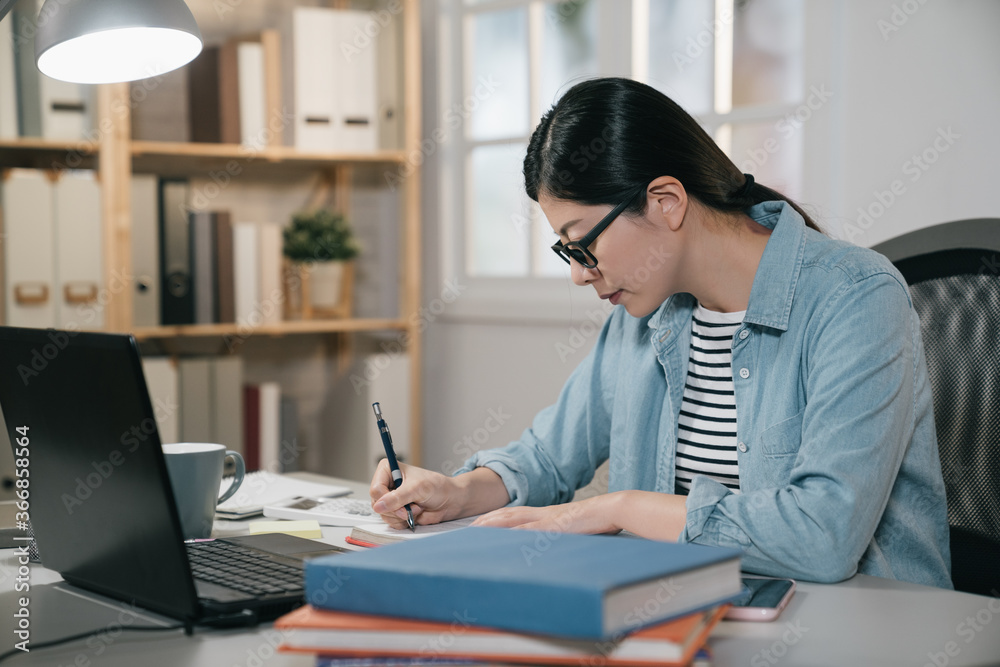 Foto de Female student taking notes from book at home. Young asian ...