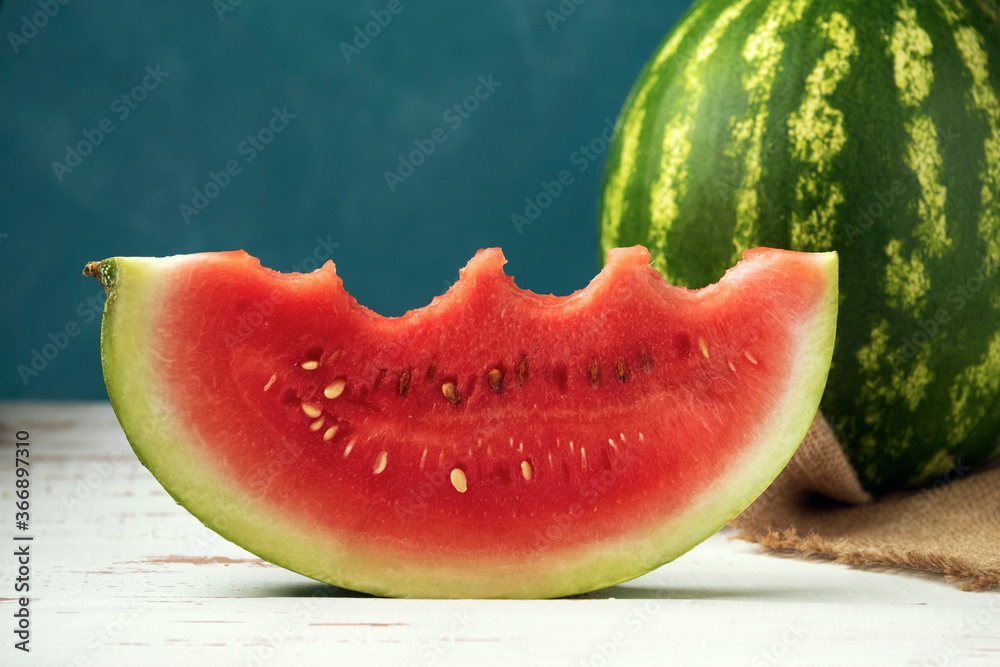 Bitten slice of watermelon with whole watermelon fruit on white wooden ...