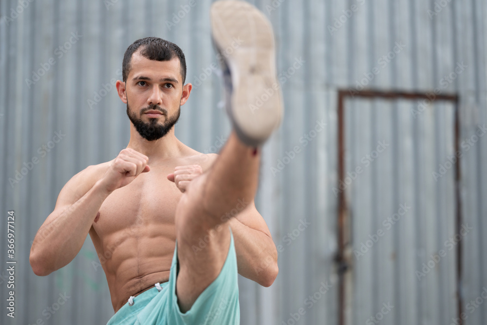 Athlete is fighting with a shadow. Kickboxer trains kicks in the street ...