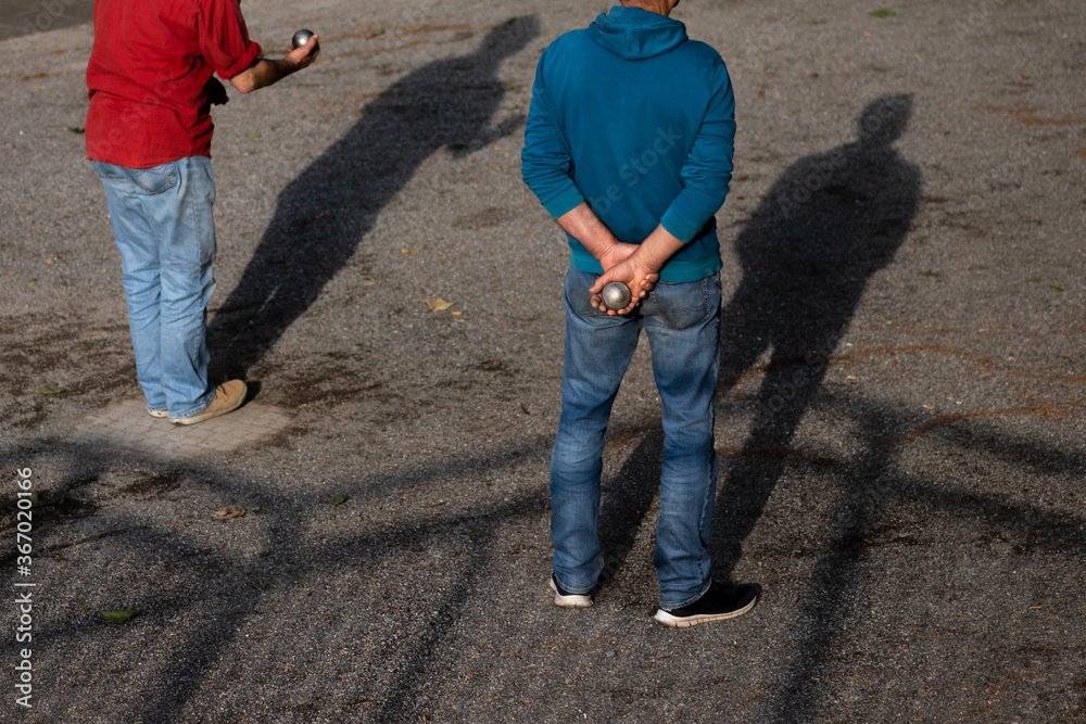 Two elderly men playing a game of boules in the gravel in urban ...