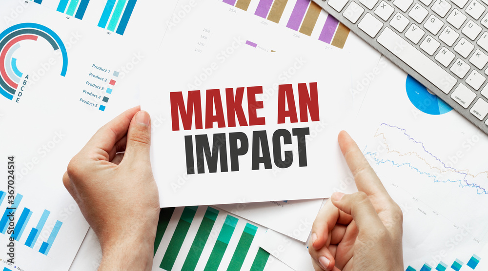 Businessman holding a card with text MAKE AN IMPACT. Keyboard, diagram ...