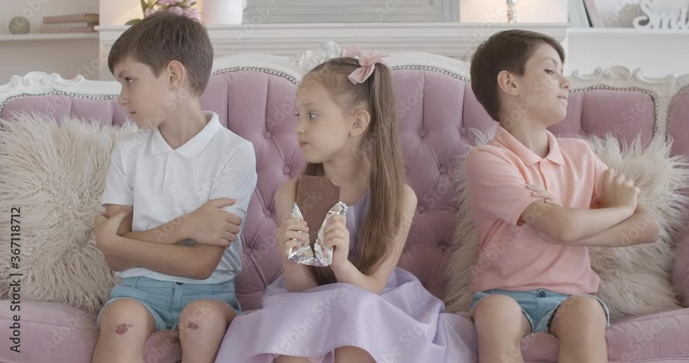 Portrait of greedy little girl chewing chocolate bar as brothers ...