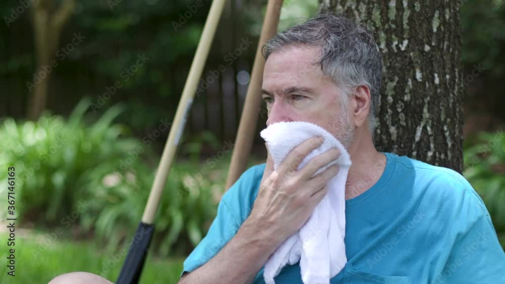 An older man who is sweating profusely from working in his yard shows ...