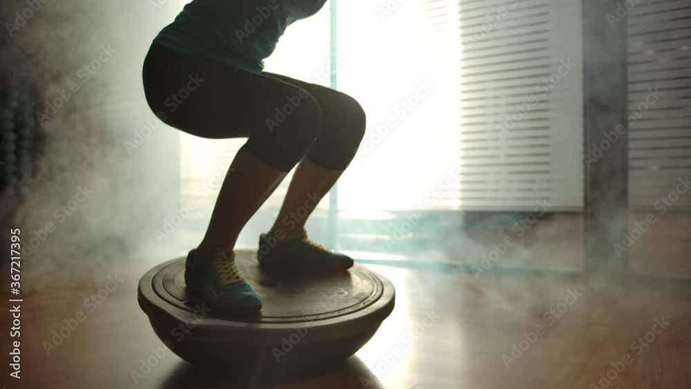 Sporty girl squatting on the hemisphere in the gym. Hard physical ...