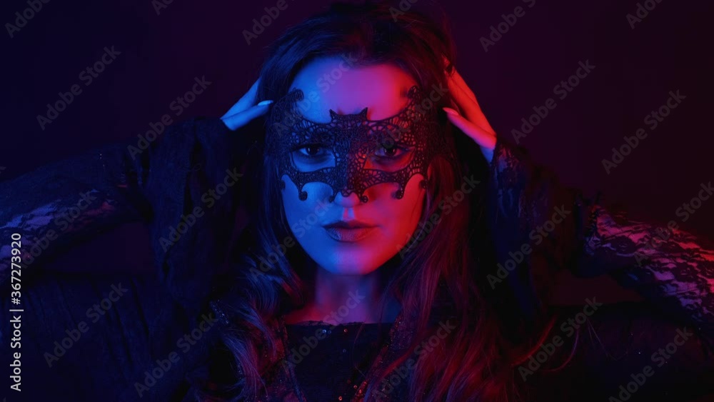 Magic witch in cloak looking at camera at dark background on halloween ...