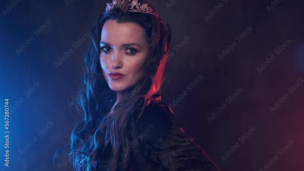 Magic witch in cloak looking at camera with smoke at background on ...