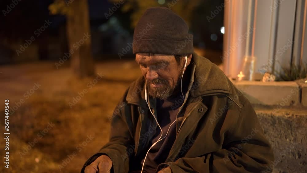 Face of lonely cold homeless man with earphones on the street at night ...