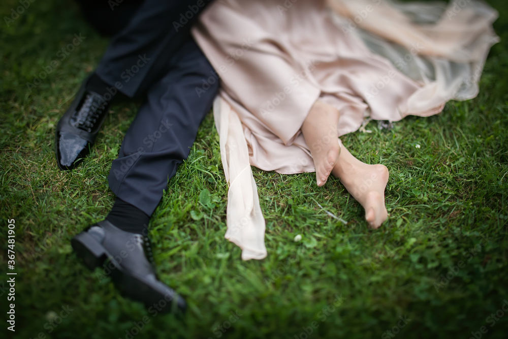 Groom the bride lie on the green grass and hug. The legs of men in ...
