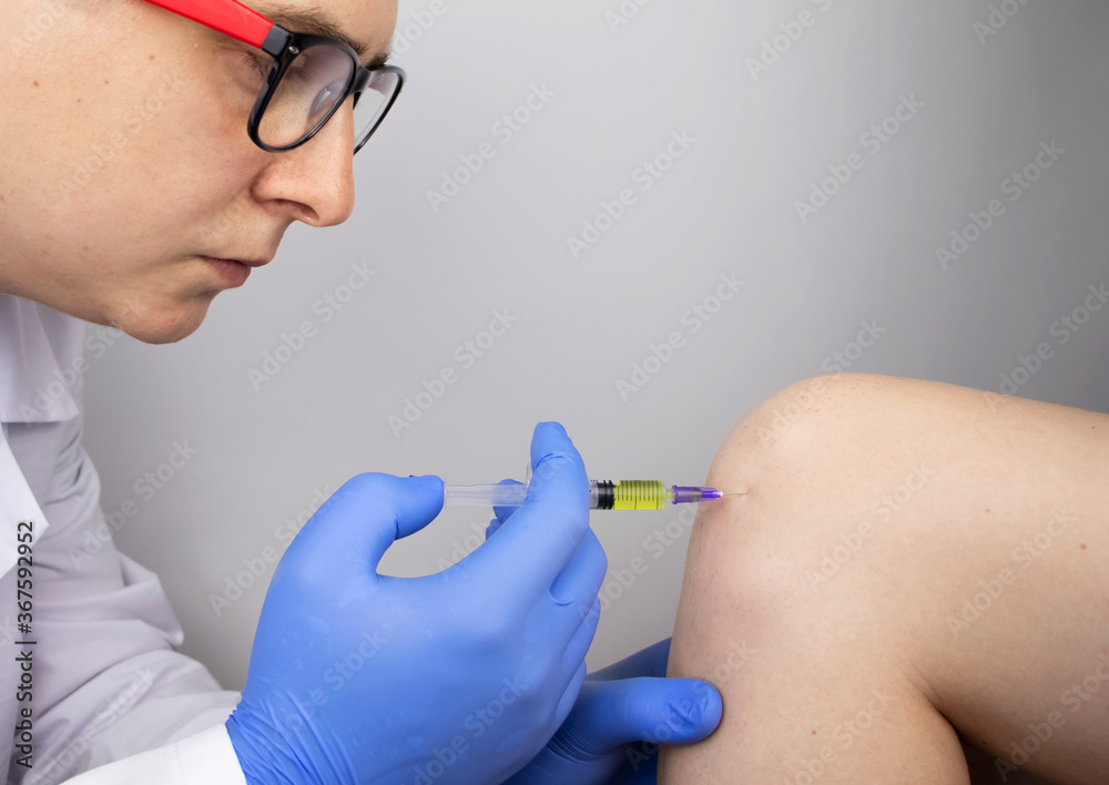 An orthopedic surgeon gives an injection in the knee. Treatment of ...