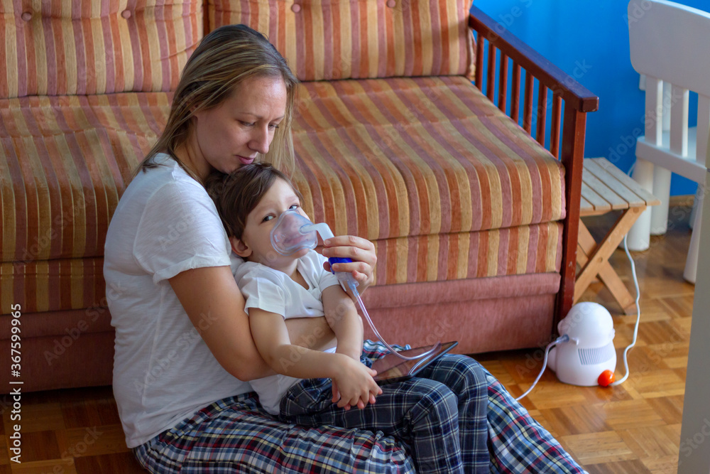 Young mother hold mask vapor inhaler to little boy breathing through ...