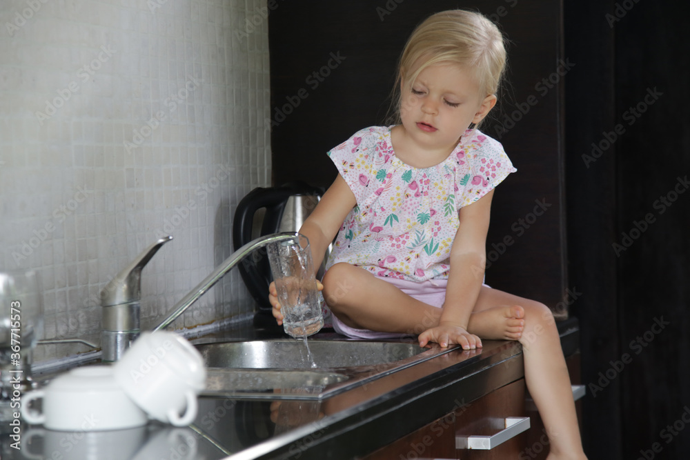 Child washing dishes in the kitchen. Cute two year old girl washes ...