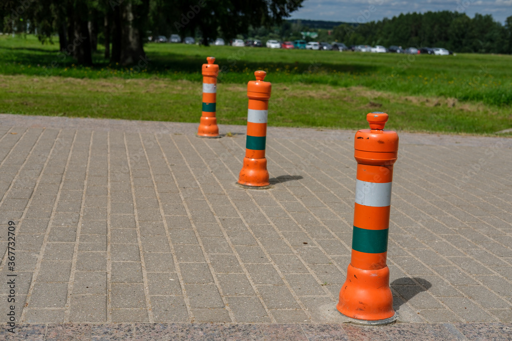 The poles are orange with green and white, stand on the paving path and ...