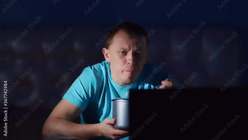 Young man eating ice cream at night and watching TV, camera movement ...