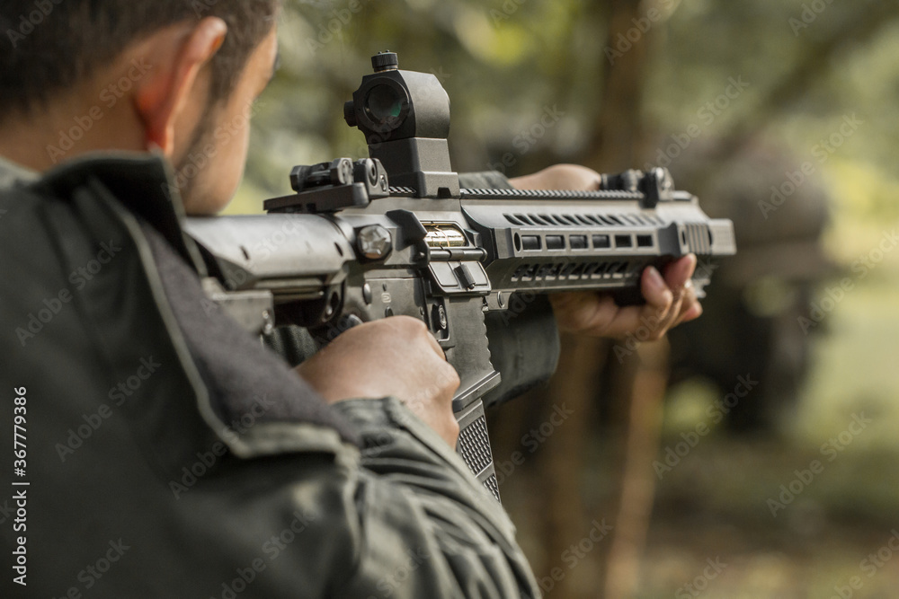 Military shooter with his precising assault rifle aiming and shooting ...