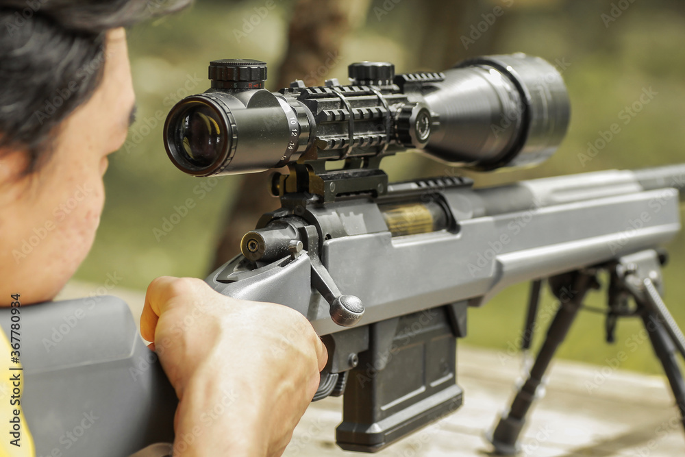 Military sniper with his precising sniper rifle aiming through scope ...