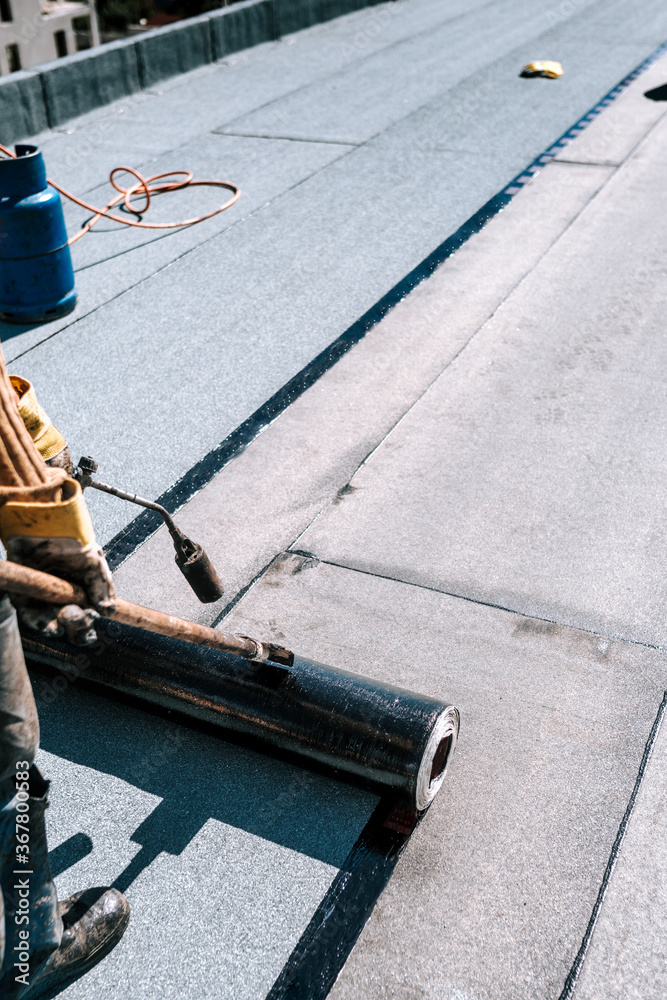 Workers waterproofing flat concrete roof using blowtorch and bituminous ...