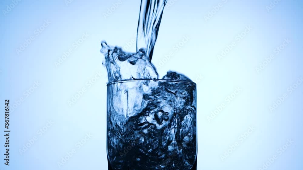 Trickle of clean mineral water and cubes of ice falling into glass then ...