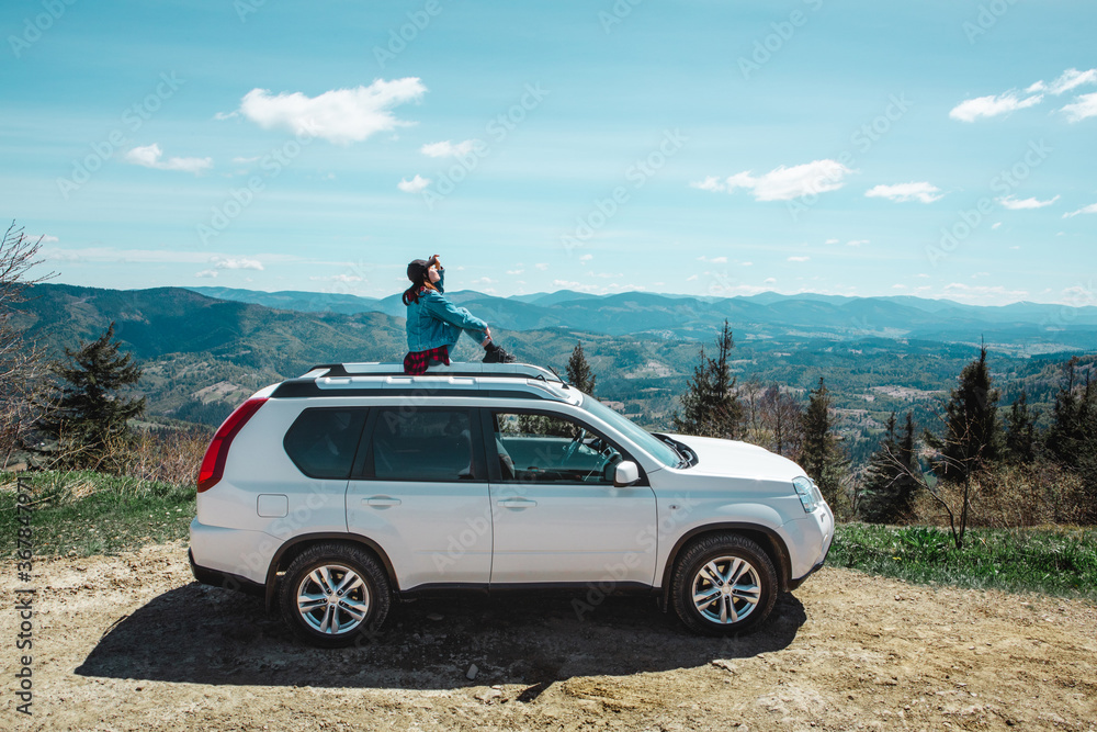 young woman sitting on the top of the suv car at mountain peak enjoying ...