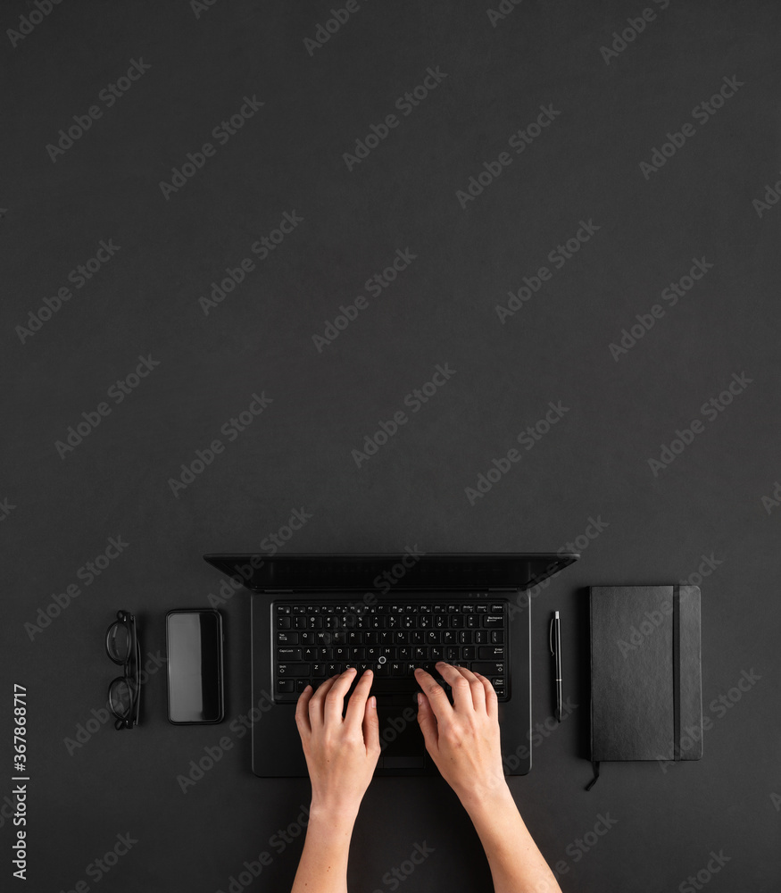 Top view of female hands working on black laptop at dark desk with copy ...