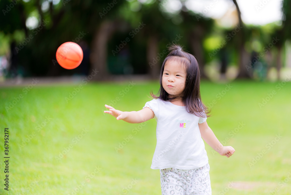 Happy Asian girl aged 3 years old throws tiny orange ball playing alone ...