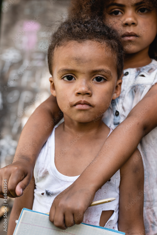 sad african american kid holding pencil and hugging poor brother in ...