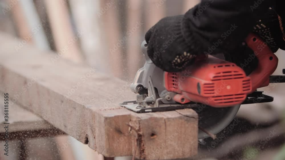 Carpenter in work clothes and gloves neatly cuts piece of board with ...