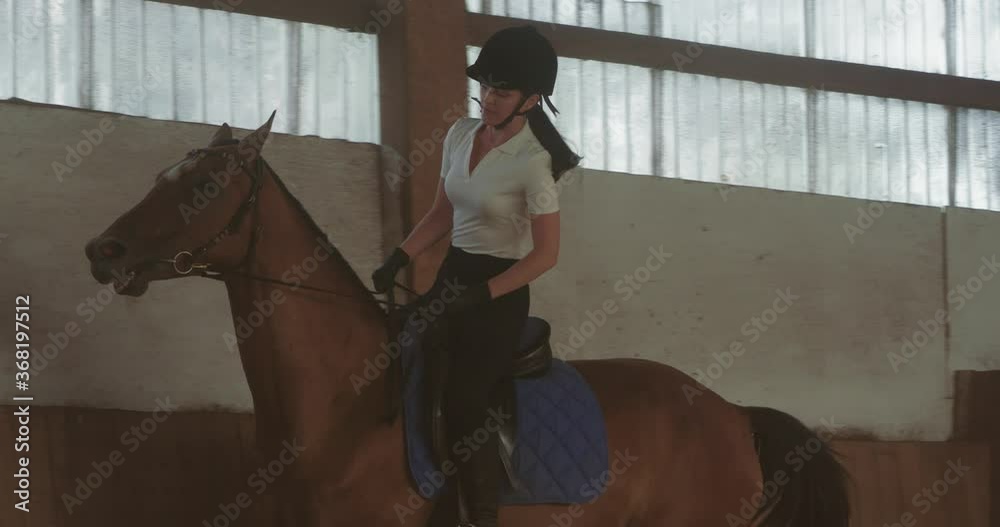Young woman trains riding a horse in a covered hangar, girl rides a ...