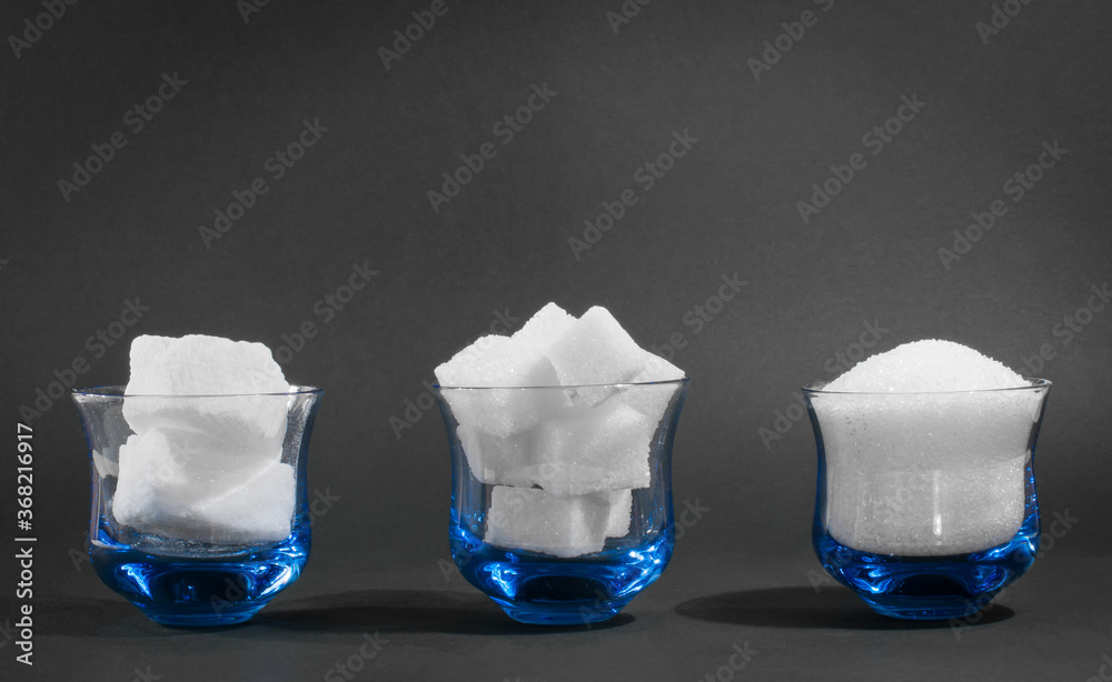 three blue cups with white sugar of different varieties on a black ...