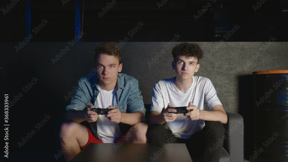 Two young friends playing action video game in the living room sitting ...