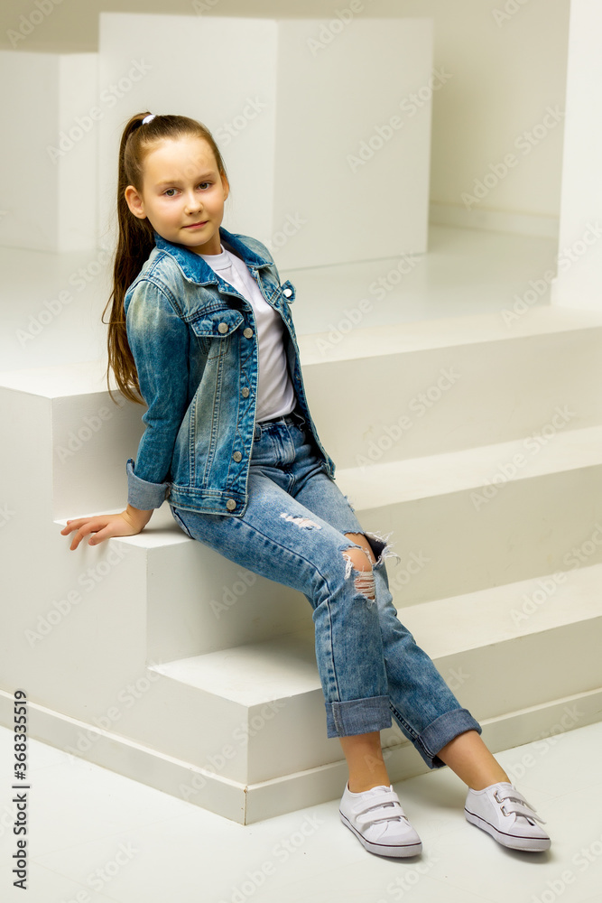 Cute little girl is sitting in the studio on the white stairs. style ...