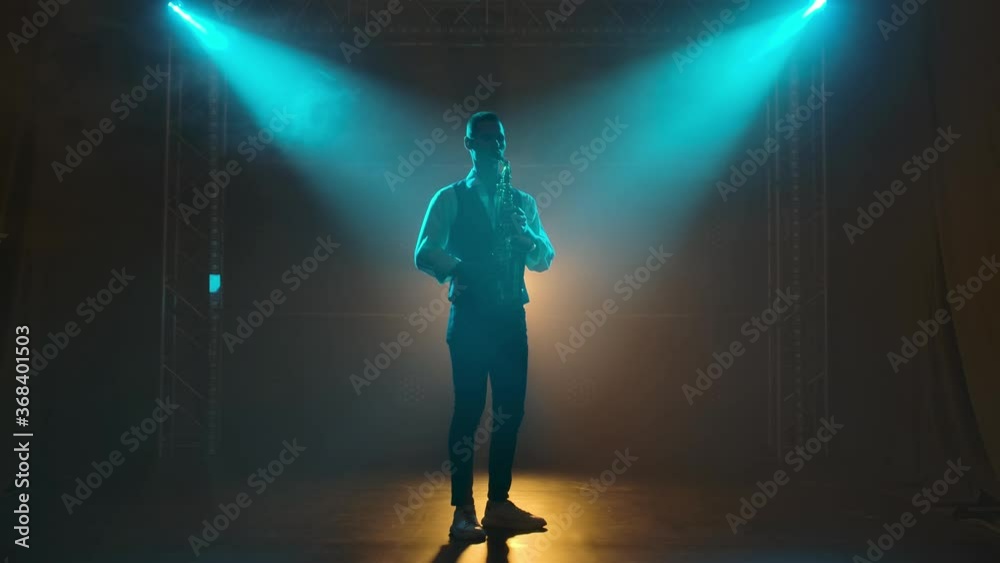 Silhouette a young stylish guy plays the golden shiny saxophone in the ...