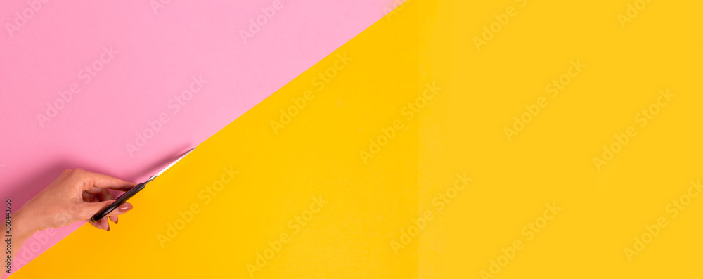 The left female hand cuts the pink-yellow background in half with ...