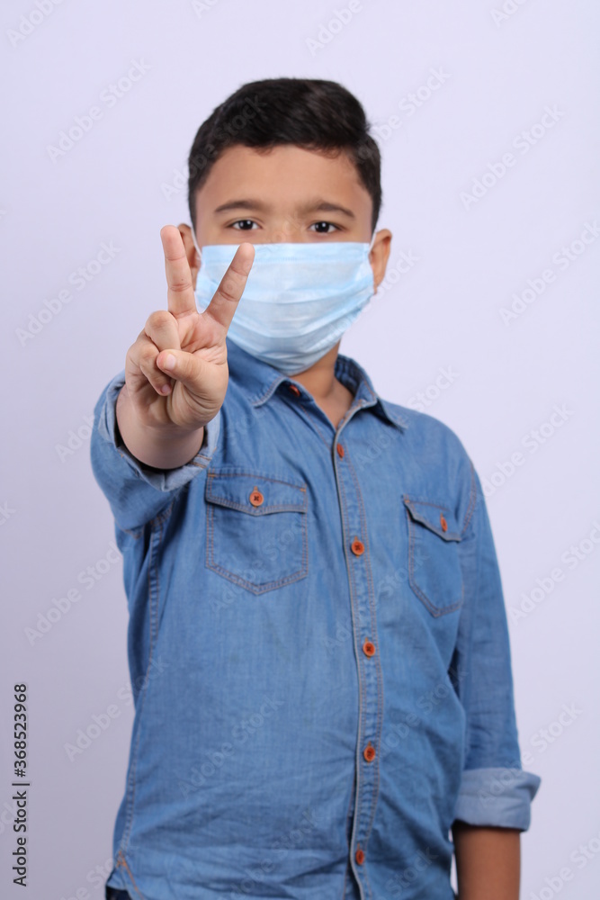Cute and smart Indian boy in surgical mask displaying victory pose. Its ...
